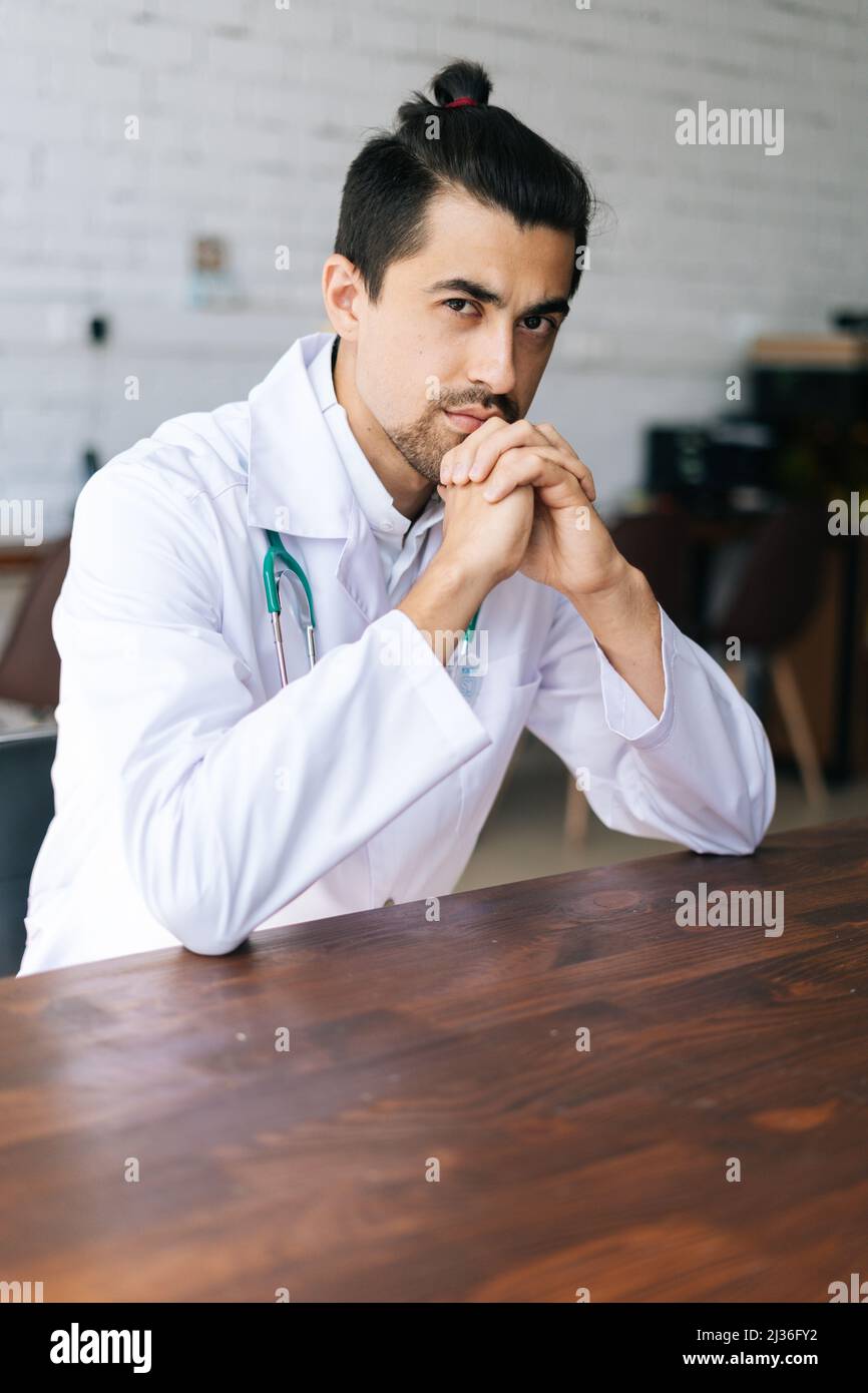 Vertical portrait of serious handsome male doctor wearing white uniform ...