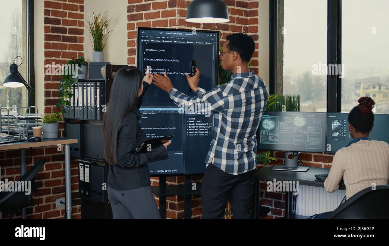 Software Engineers Analyzing Code On Wall Screen Tv Comparing Errors Using Digital Tablet Next