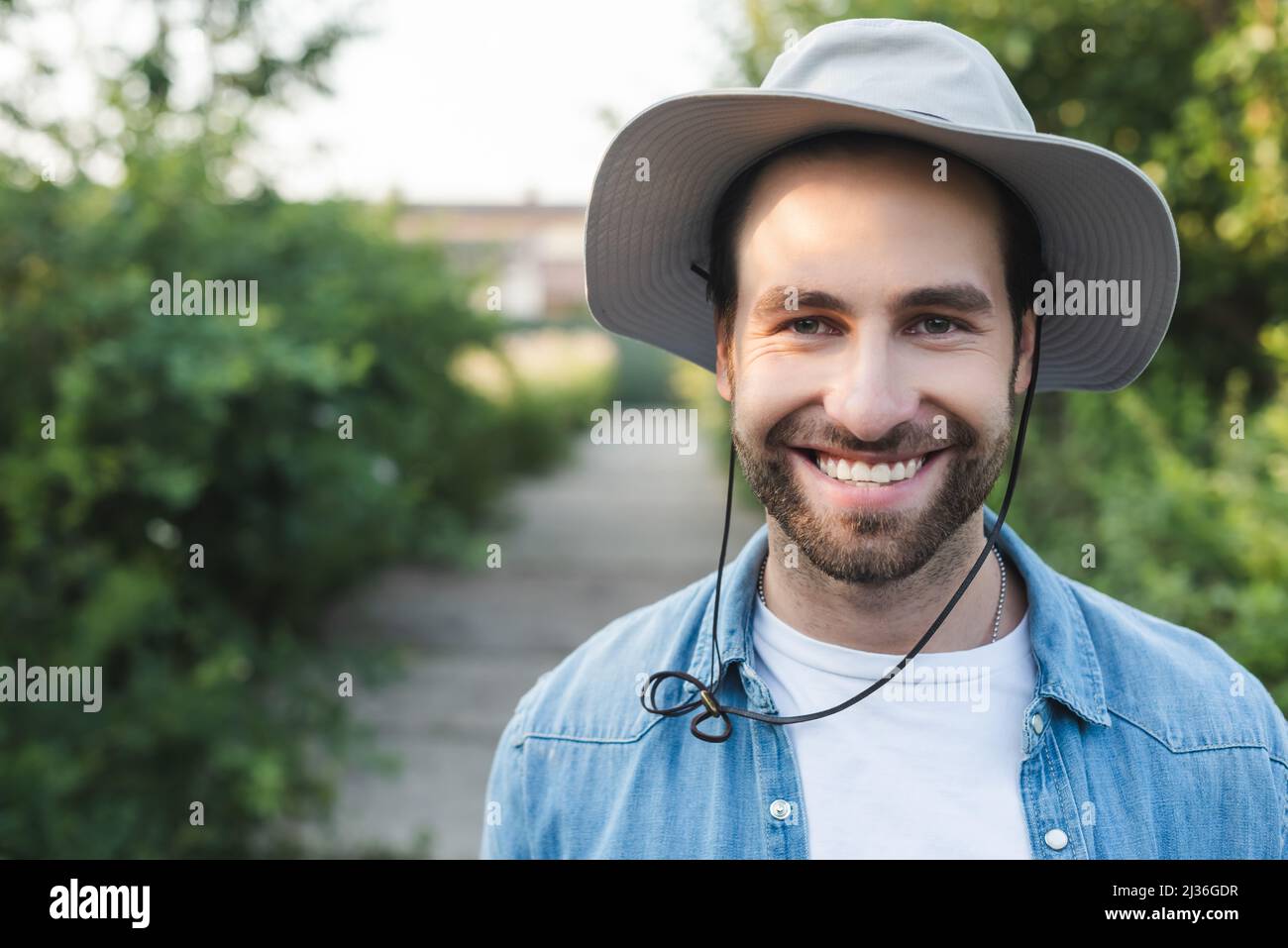 young and bearded farmer in brim hat smiling at camera outdoors Stock ...