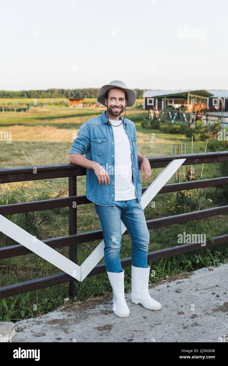 full length view of smiling farmer in denim clothes standing near ...