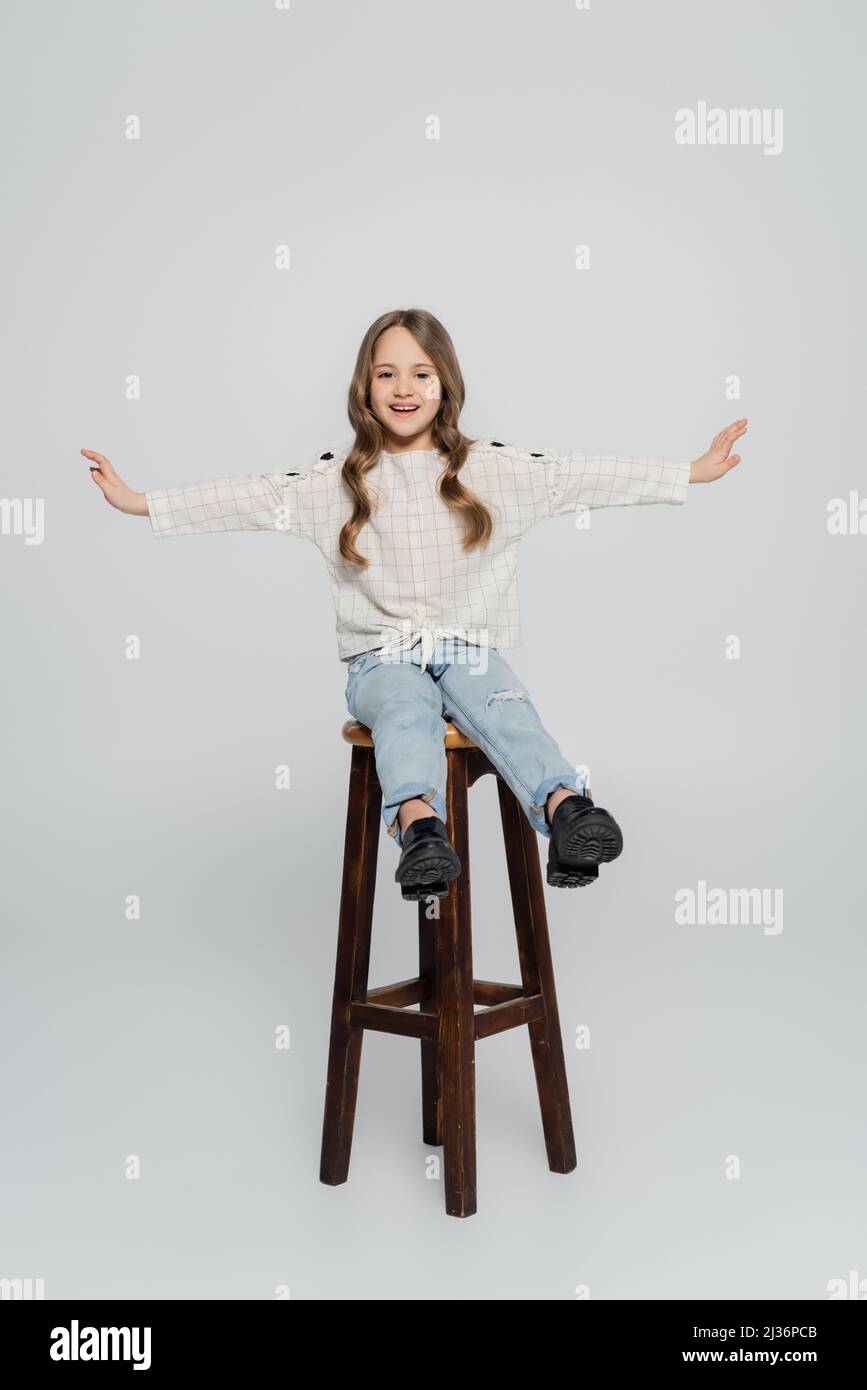 full length view of cheerful girl sitting on high stool with ...
