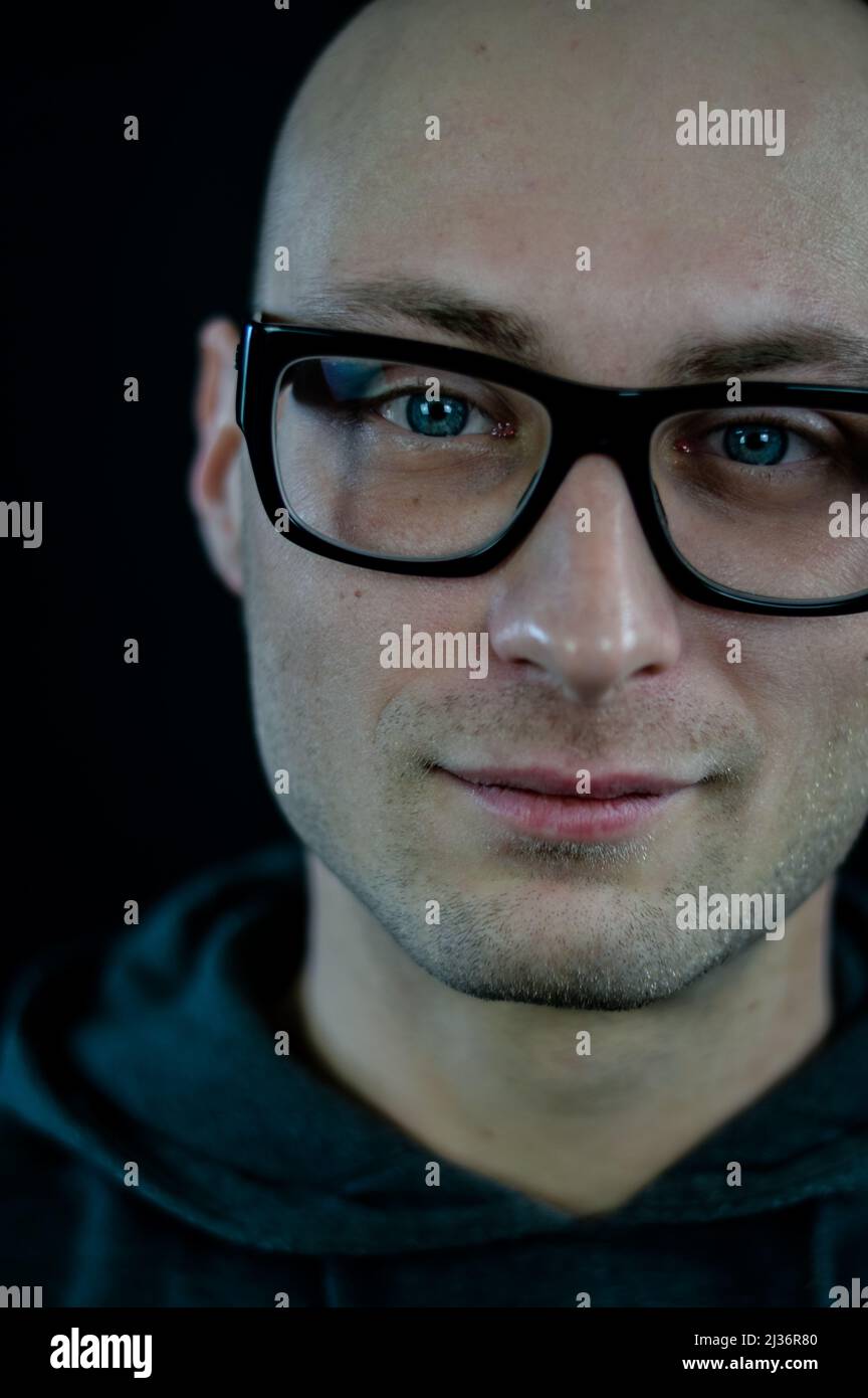 Close up portrait of a young bald man with black eyeglasses showing a ...