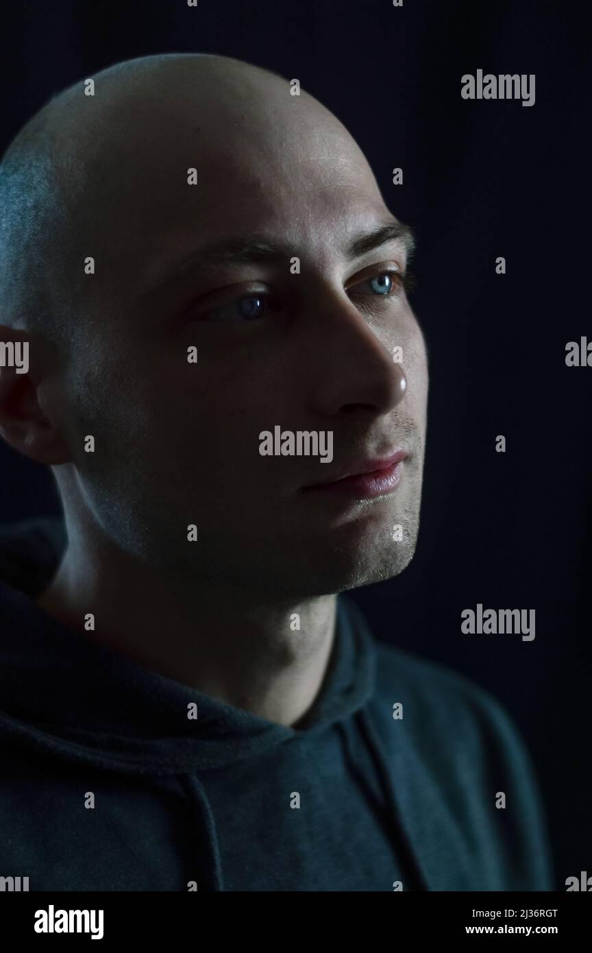 Portrait of a handsome young bald man with blue eyes who in the dim ...