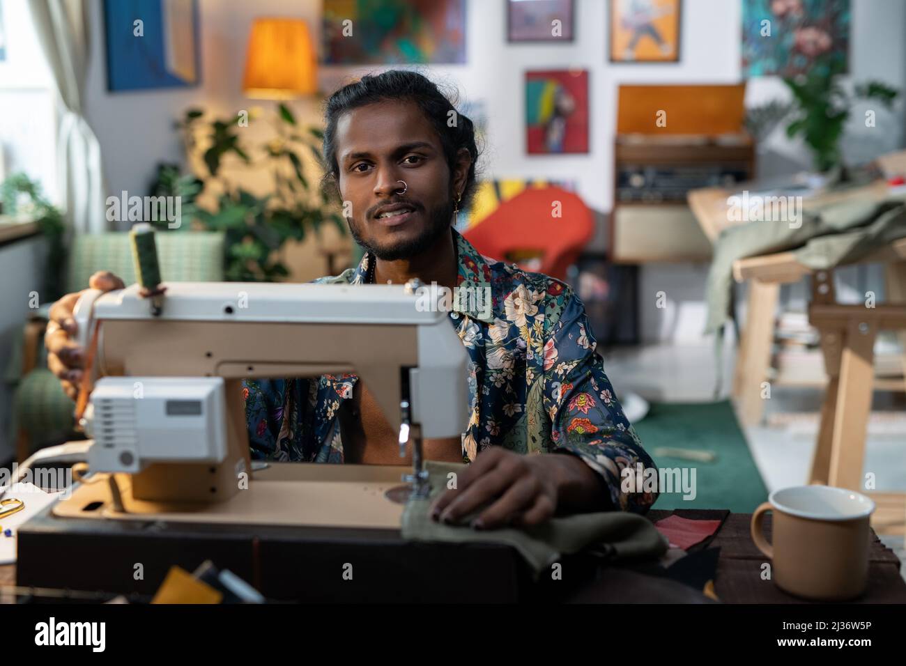 Portrait of joyful young Indian man with nose piercing sitting in front ...