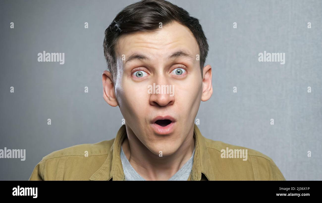 Handsome guy with stylish hairdo surprised to camera over grey ...