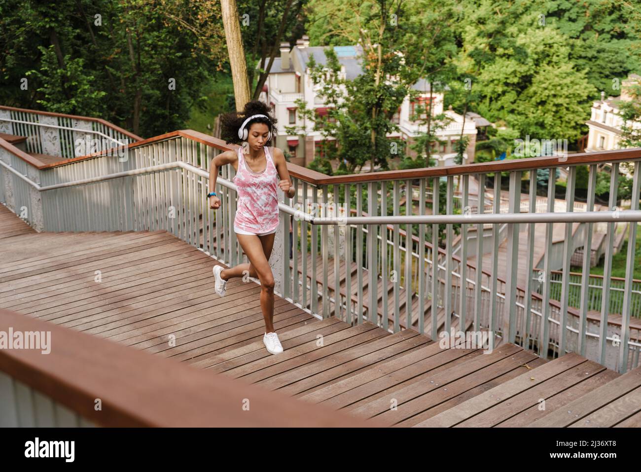 Young black woman listening music with headphones while running up ...