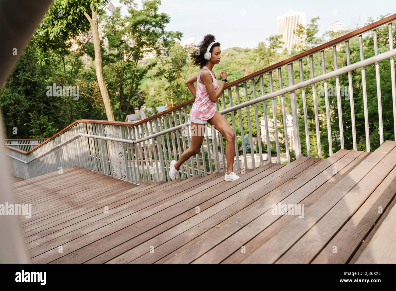 Young black woman listening music with headphones while running up ...
