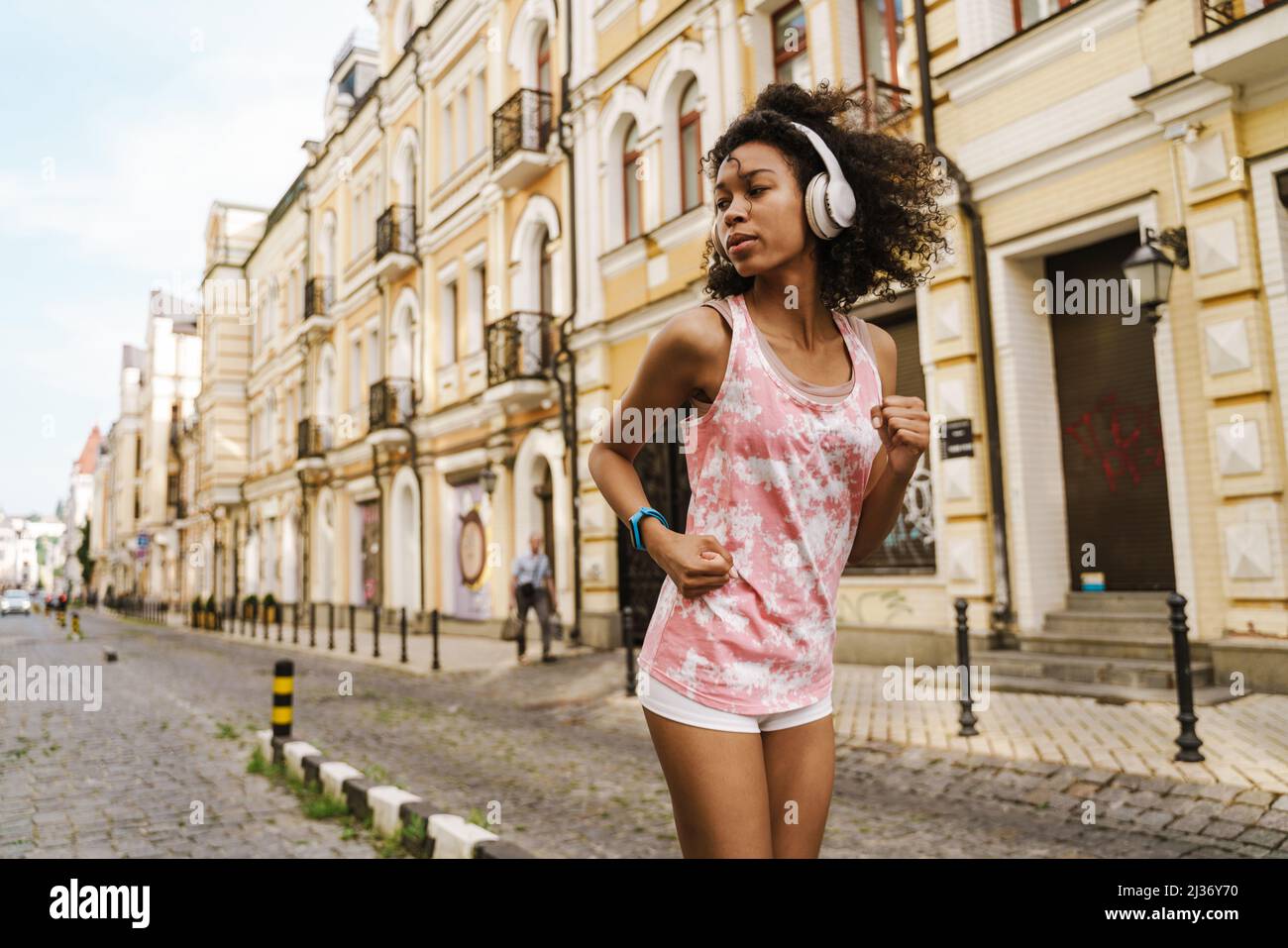 Young black woman listening music with headphones while running on city ...