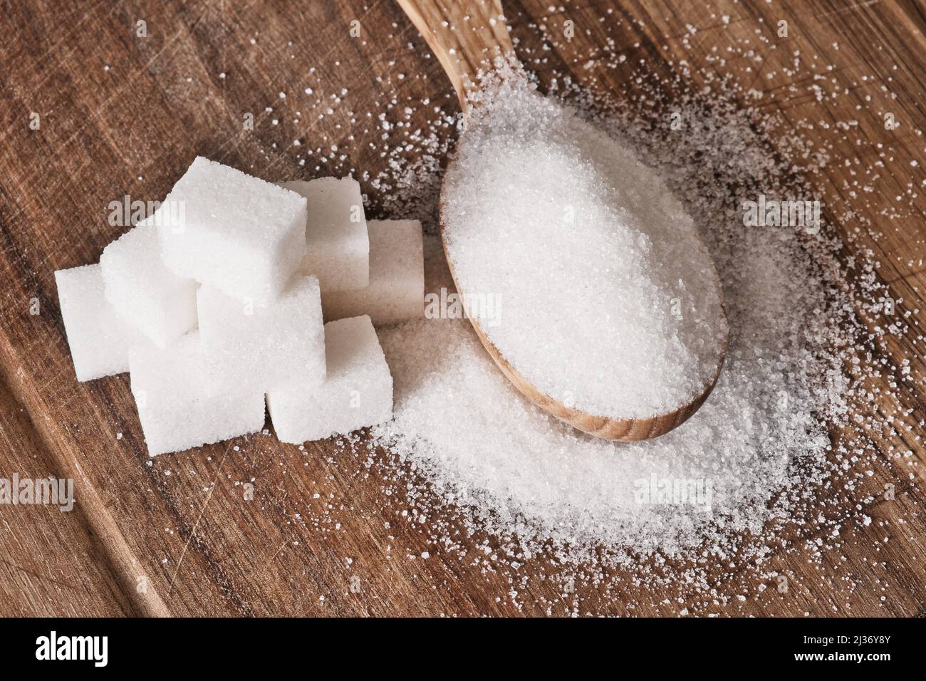 Granulated sugar in wooden spoon and sugar cubes stacked in pyramid on ...