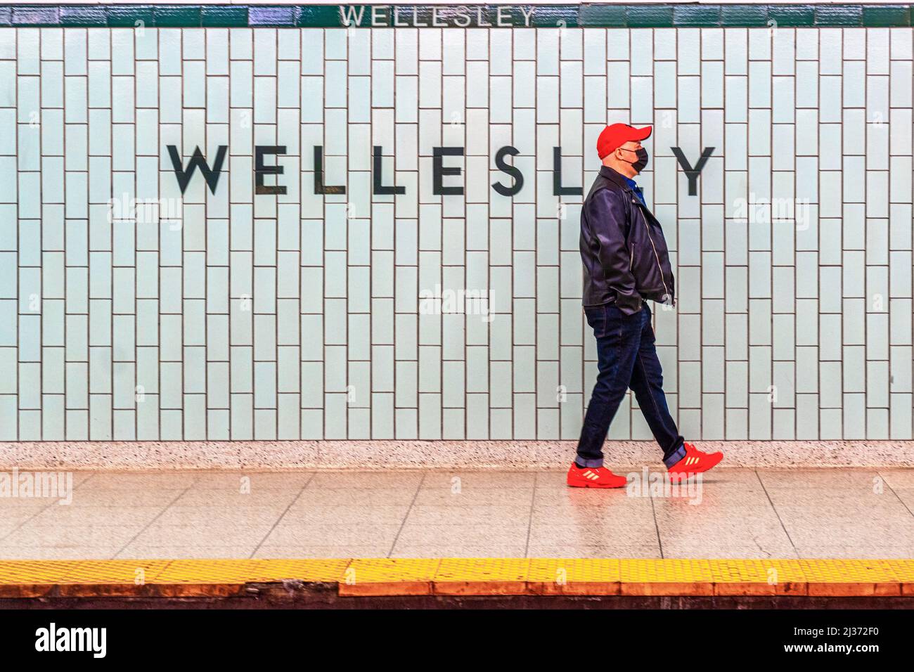 A man wearing a face mask and red shoes walks in the platform of ...