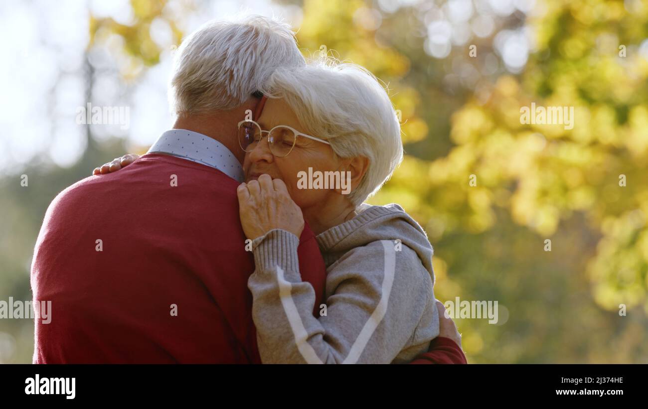 Portrait of aged Caucasian married couple tightly hugging in the park ...