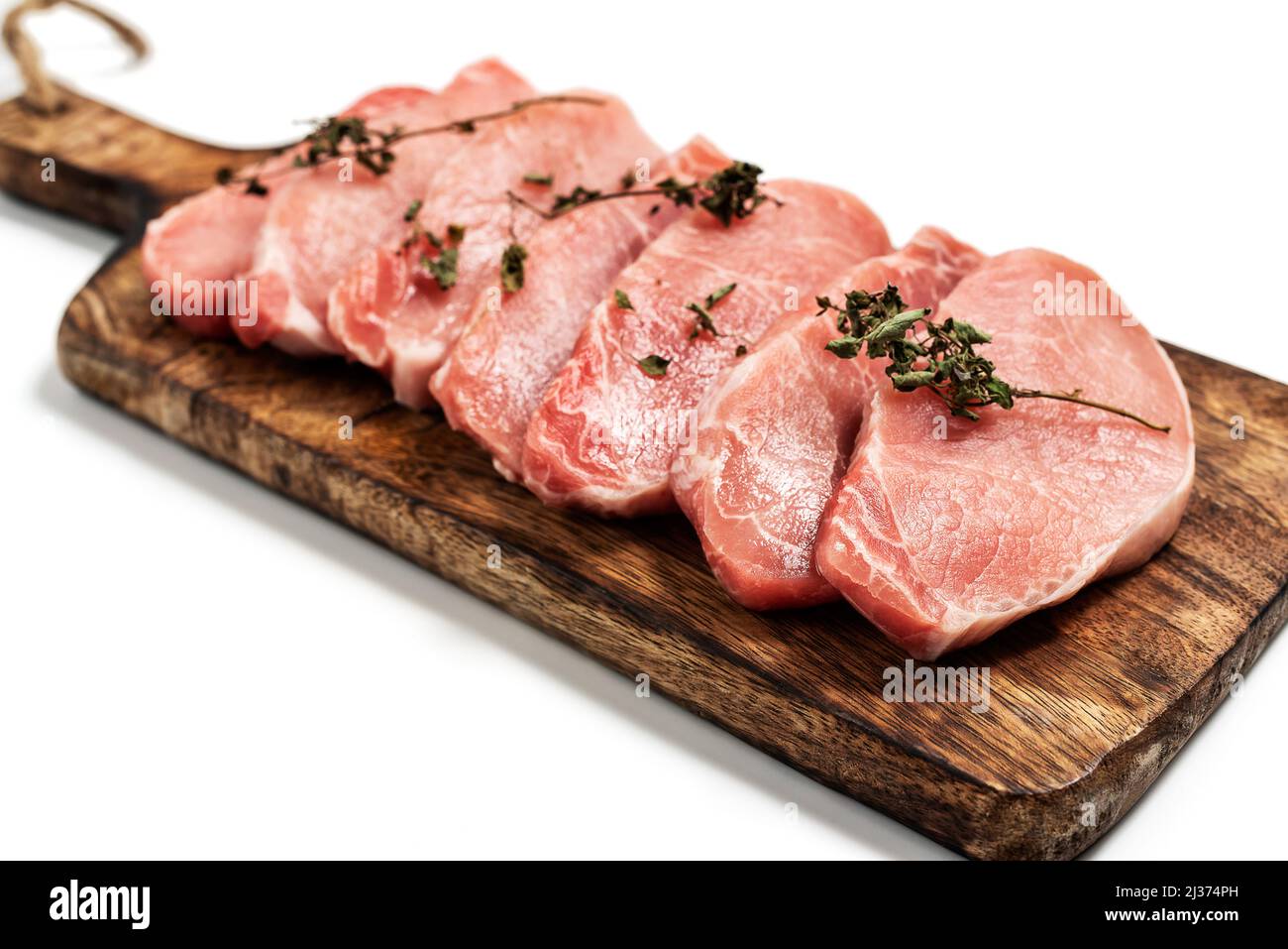 Raw pork sliced meat on wooden board on white background with dry basil ...