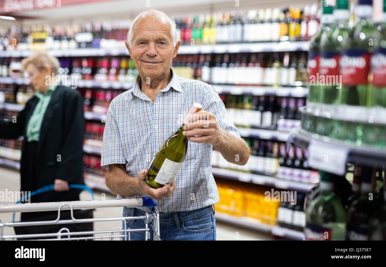mature european man chooses bottle of white wine in alcohol section of ...