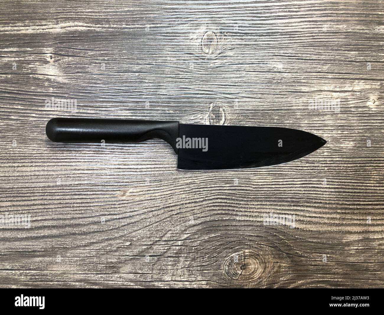 The black knife lying on the table with wooden texture. Close up image ...