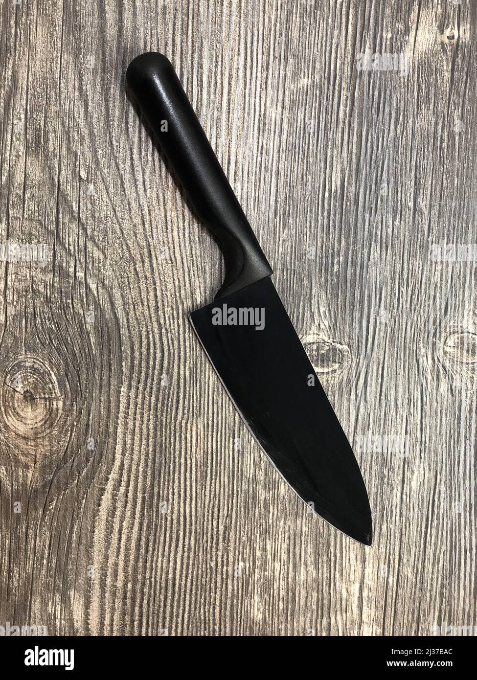 The black knife lying on the table with wooden texture. Close up image ...