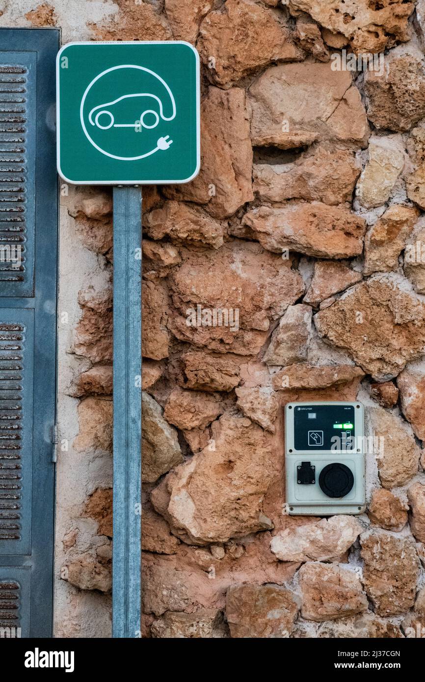 A vertical shot of a car charging station sign on a stone wall ...