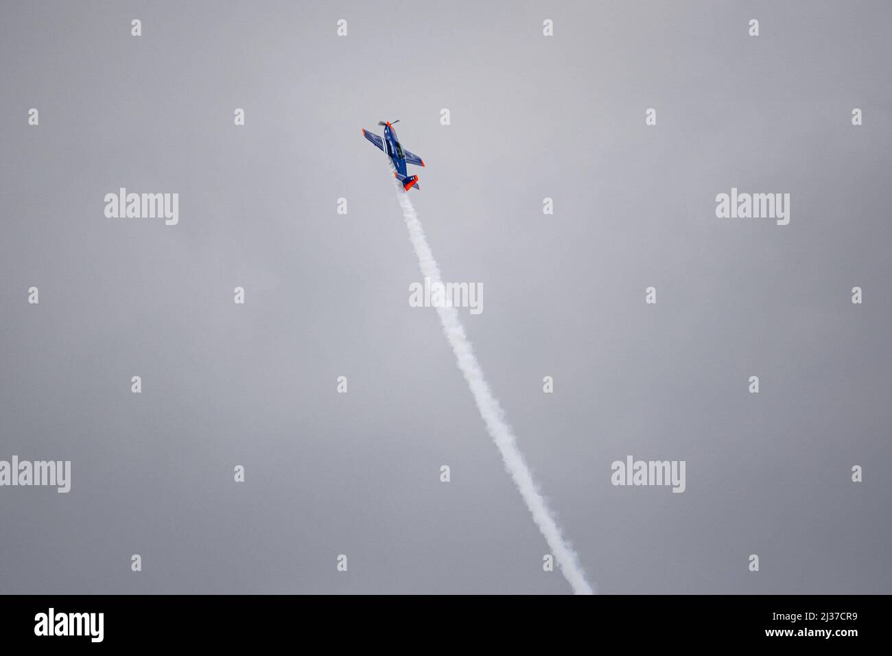 A low angle shot of a blue orange jet flying in a foggy sky for a sport ...