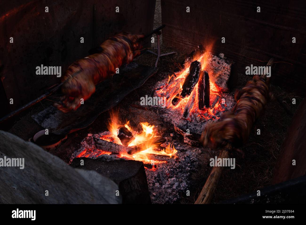 Two whole pig roasting on spit next to fire with sparks in long ...