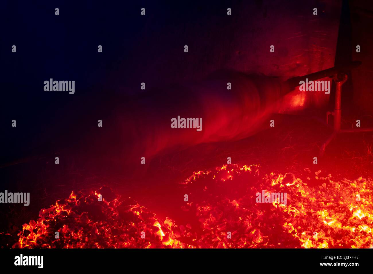 Whole pig spinning on a spit above fire ember in heat and smoke at ...