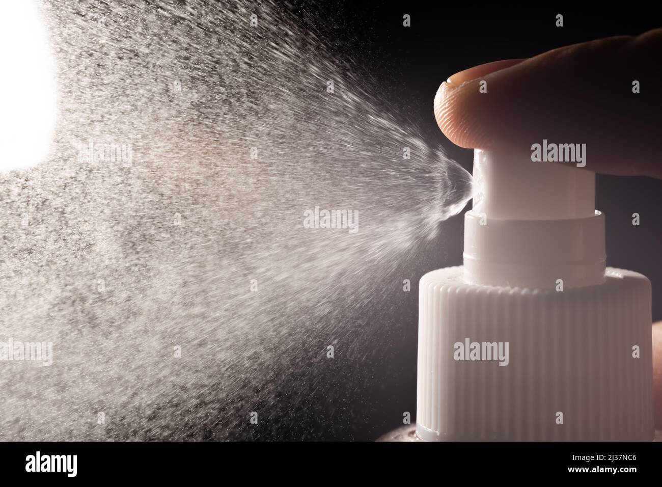 Liquid sprayed from a spray bottle towards a light source. A finger is ...