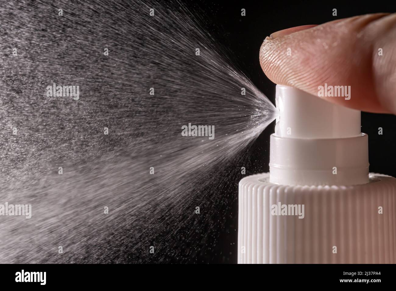 Liquid spraying from a spray bottle on a black isolated background. A ...