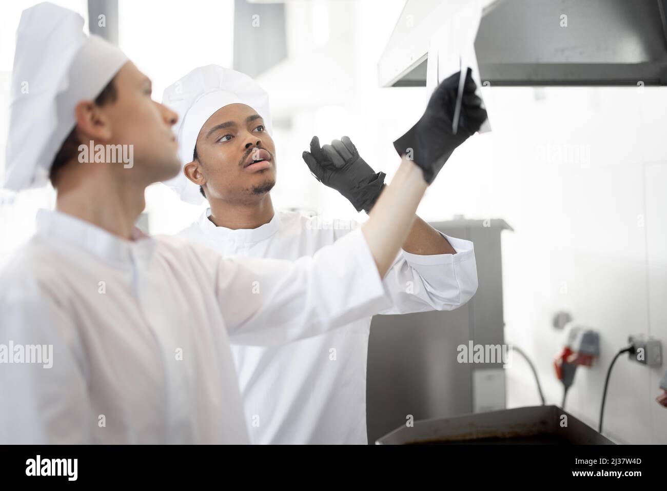 Two well-dressed chefs look on printed checks with orders while cooking ...