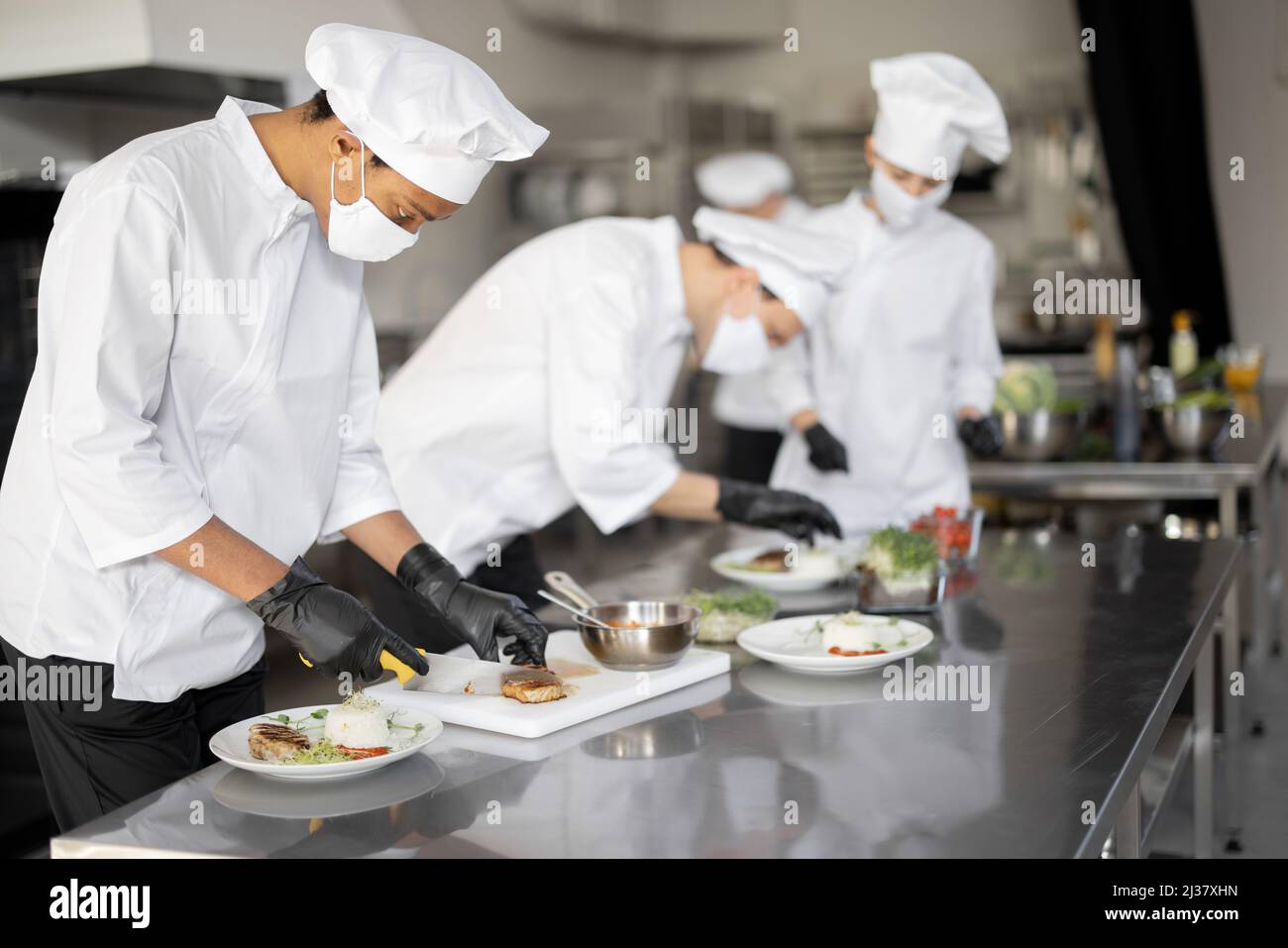 Multiracial group of cooks finishing main courses while working ...