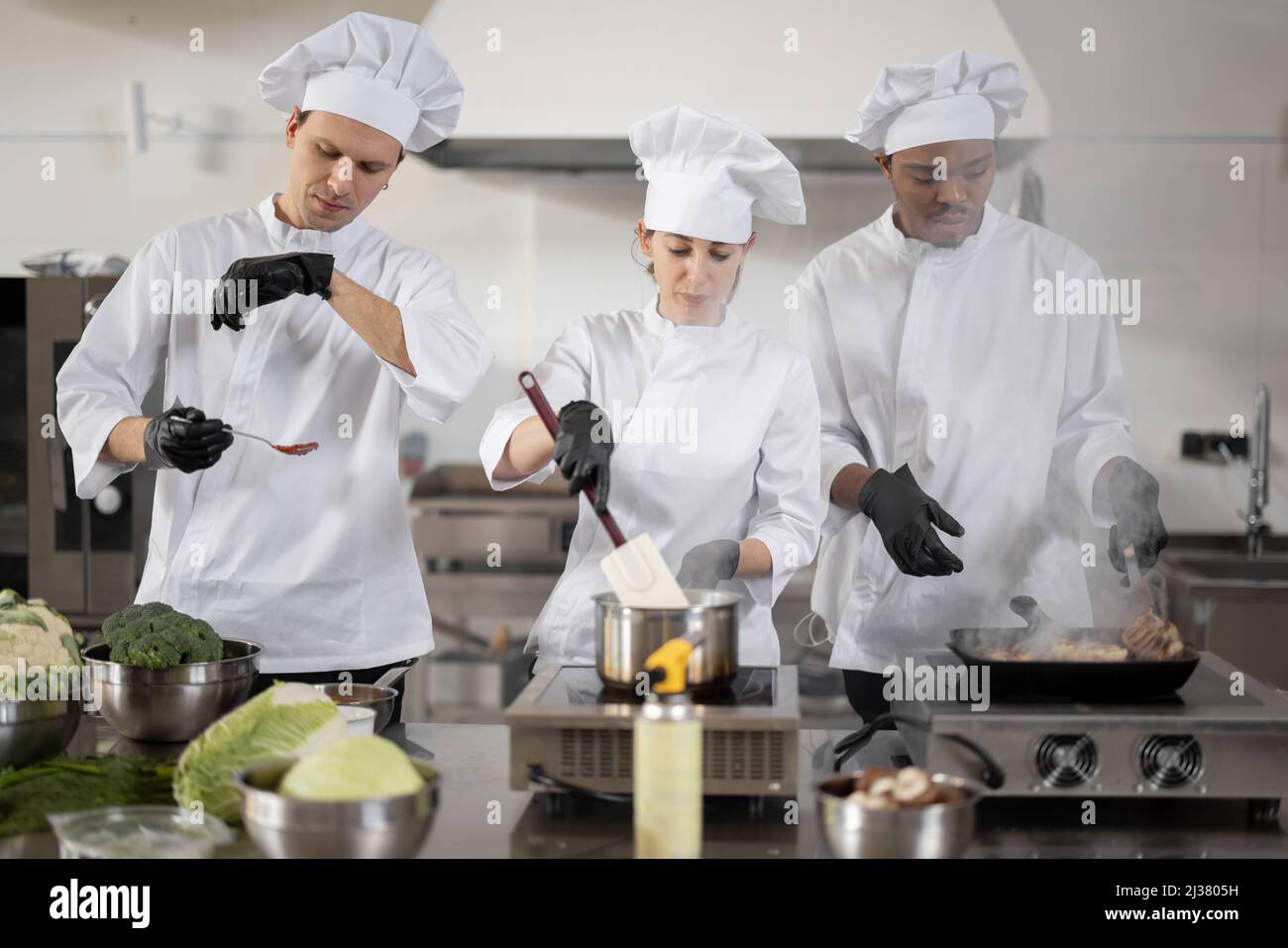 Multiracial team of three cooks in uniform cooking together in the ...