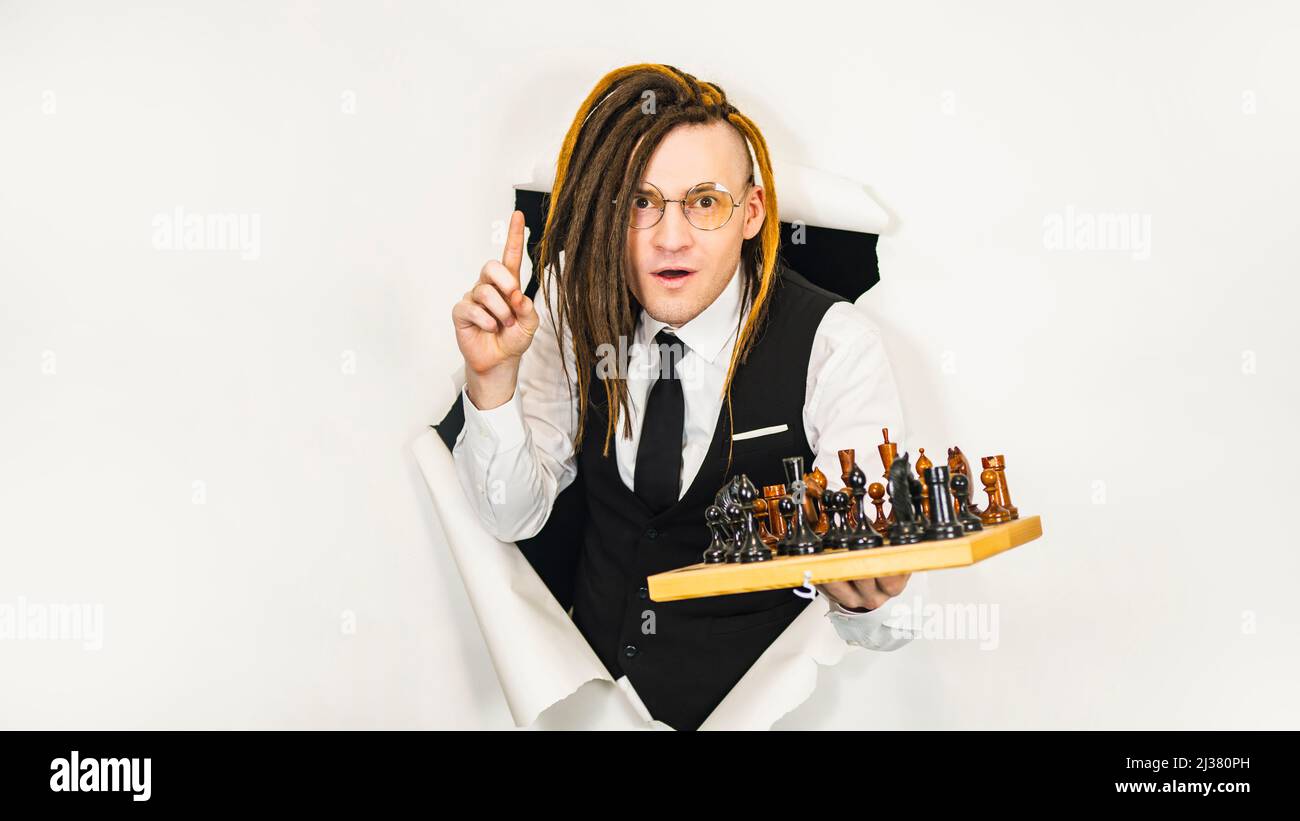 Young man in glasses with dreadlocks plays chess in hole of white ...