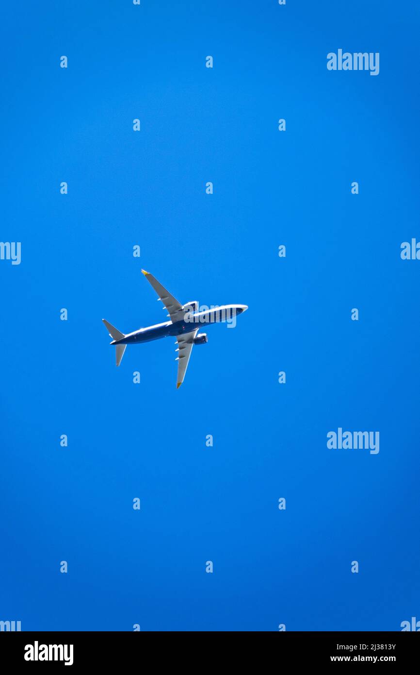 Airplane flying through bright blue sky Stock Photo - Alamy