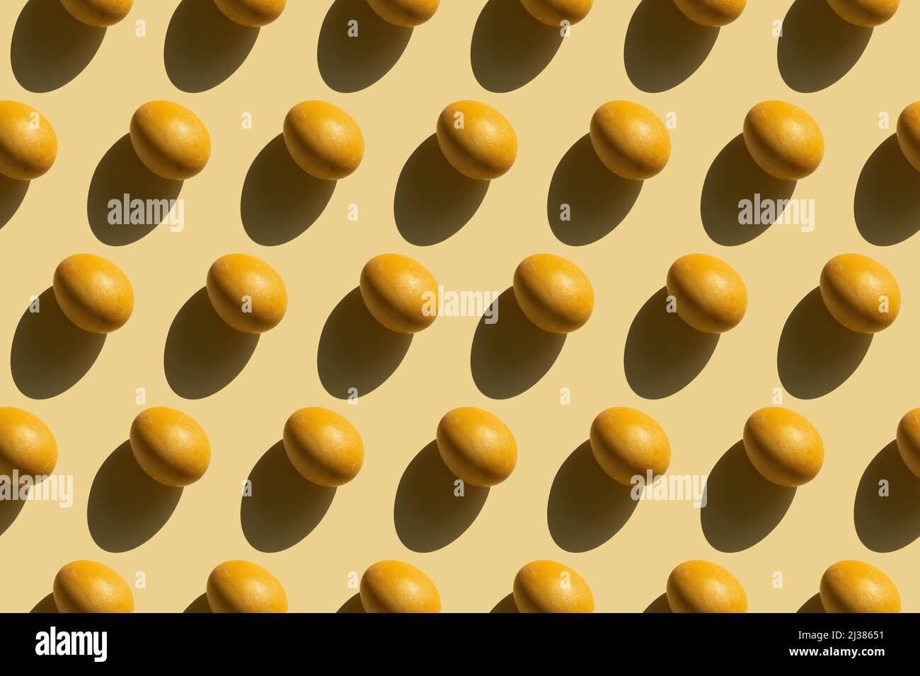 Repeating painted yellow eggs with a hard shadow on a yellow background ...