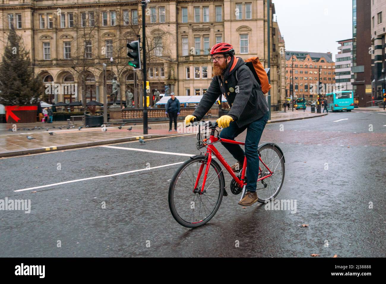 Commuter cyclist cycling through Leeds city centre wearing a red helmet ...