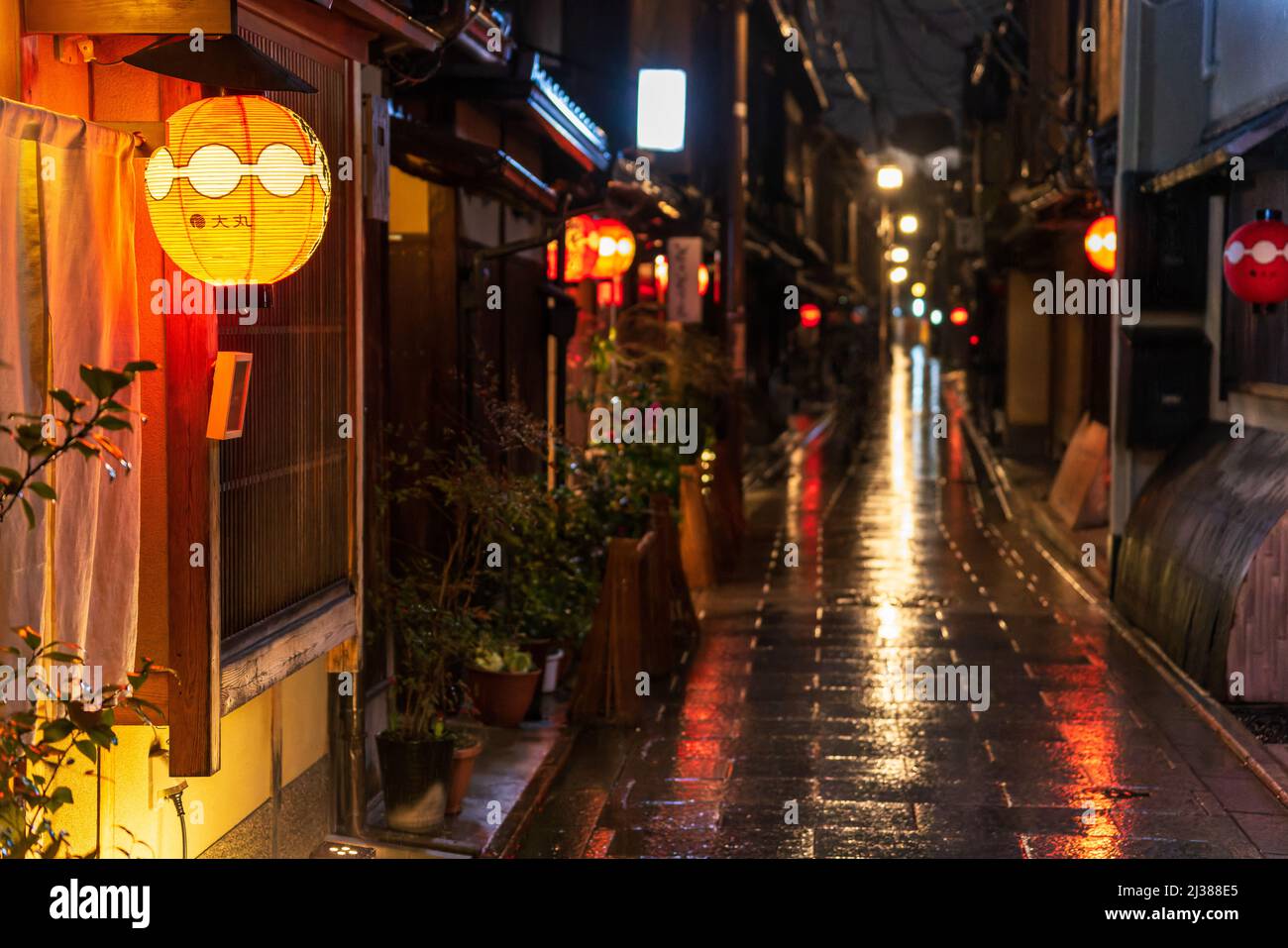 Red lantern illuminates entryway on dark Japanese street after rain ...