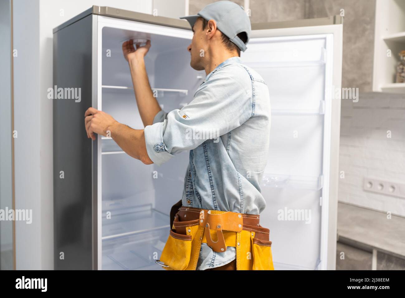 young repairman with tool belt looking at broken refrigerator Stock ...