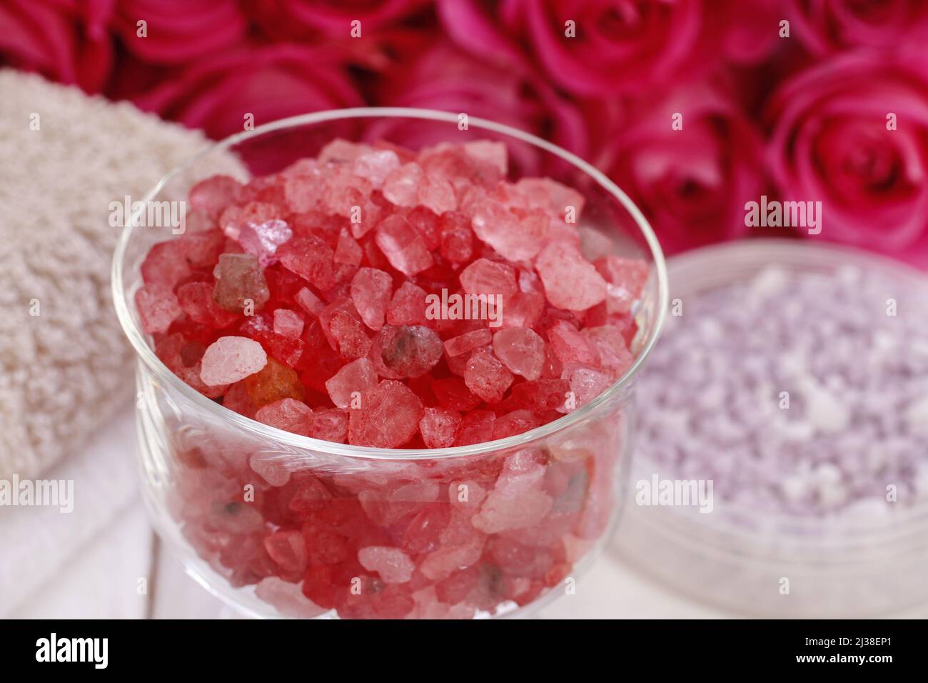 Glass bowl with red sea salt. Pink roses in the background. Spa time ...