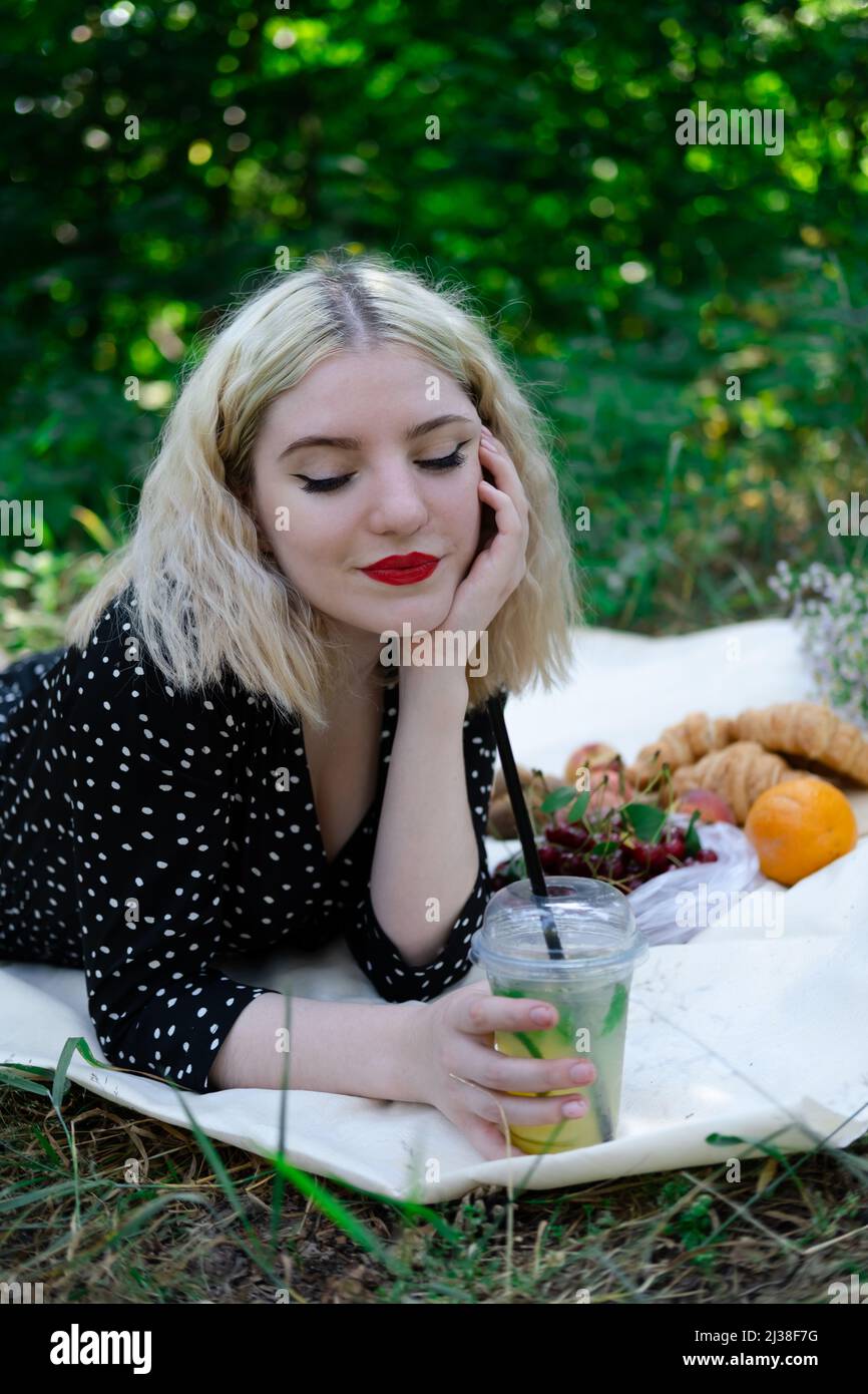 pretty blonde girl on a picnic in a forest or park with lemonade ...