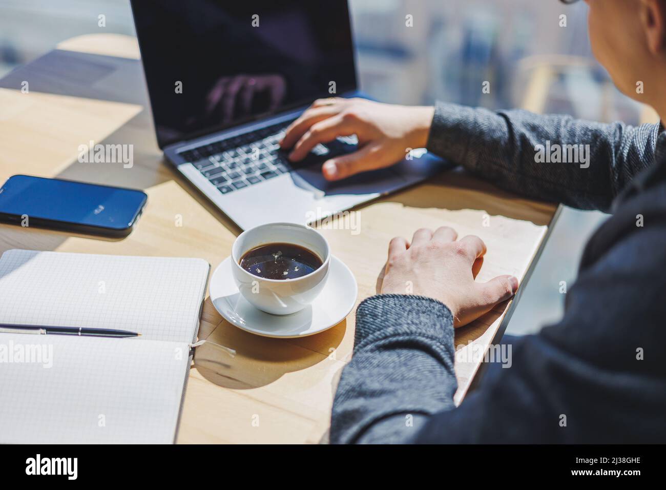 A man using a laptop while sitting at a wooden table. Male hands typing ...