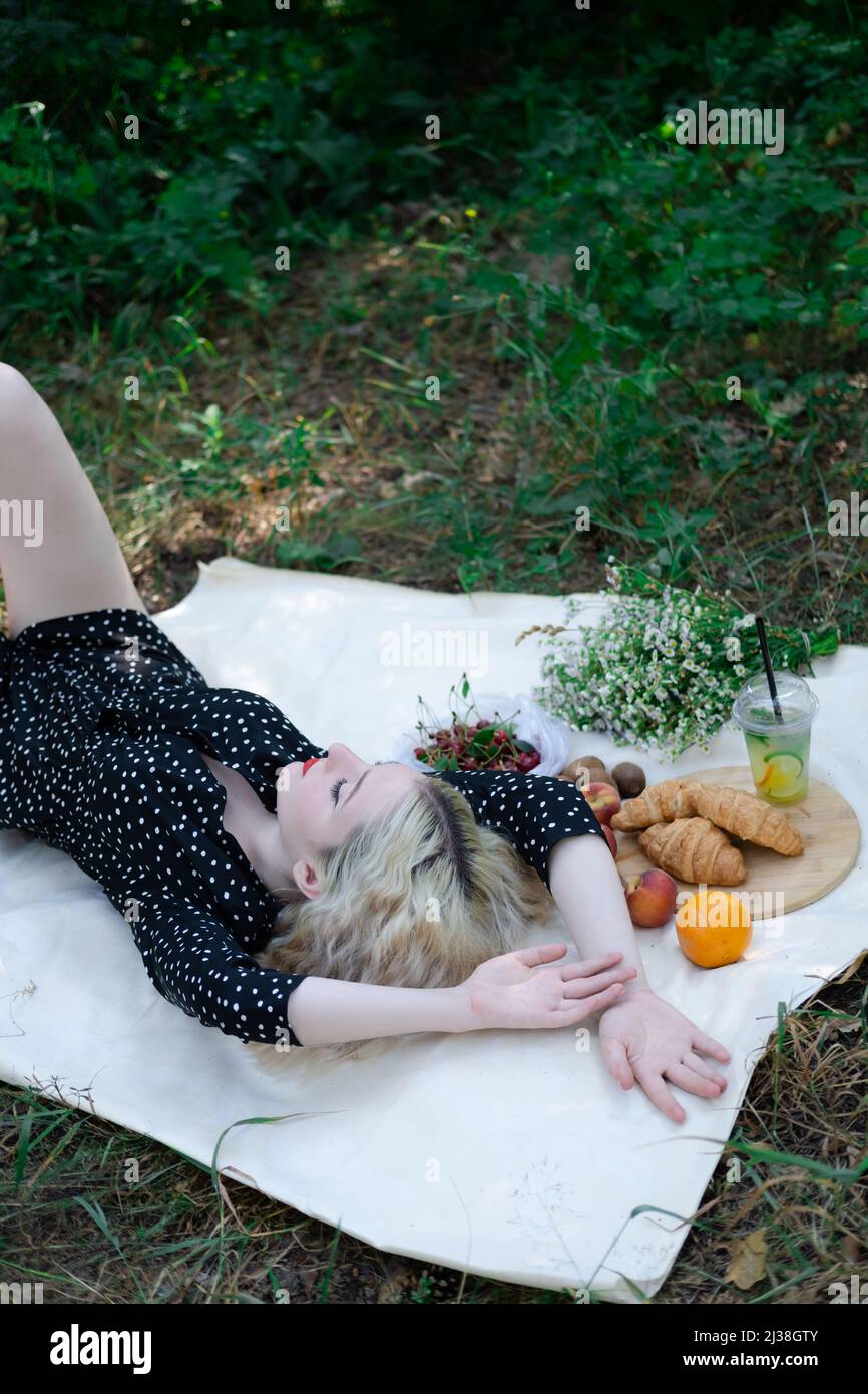 charming blonde young woman on a picnic on plaid in park with tasty ...