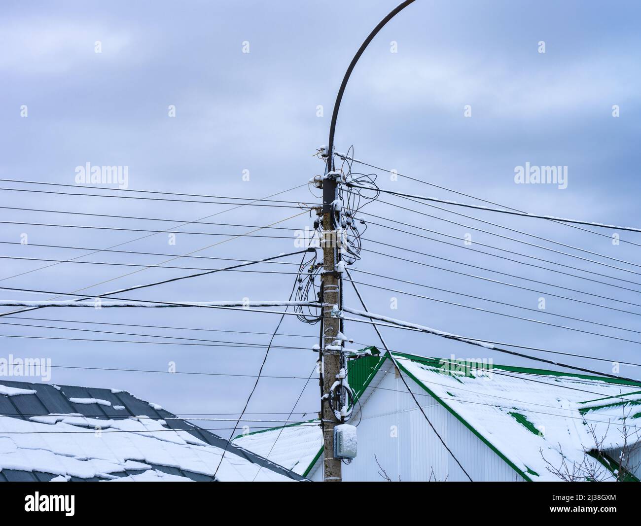 A lamp post with a lot wires on it near some snowy houses Stock Photo ...