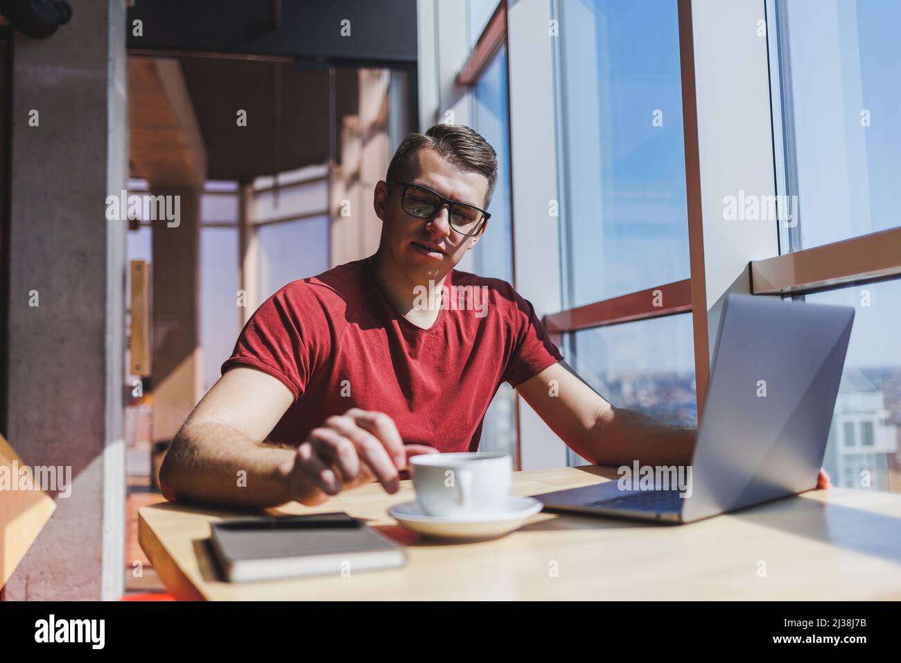 Portrait of a man, IT professional, working remotely with a modern laptop, sitting at a table ...