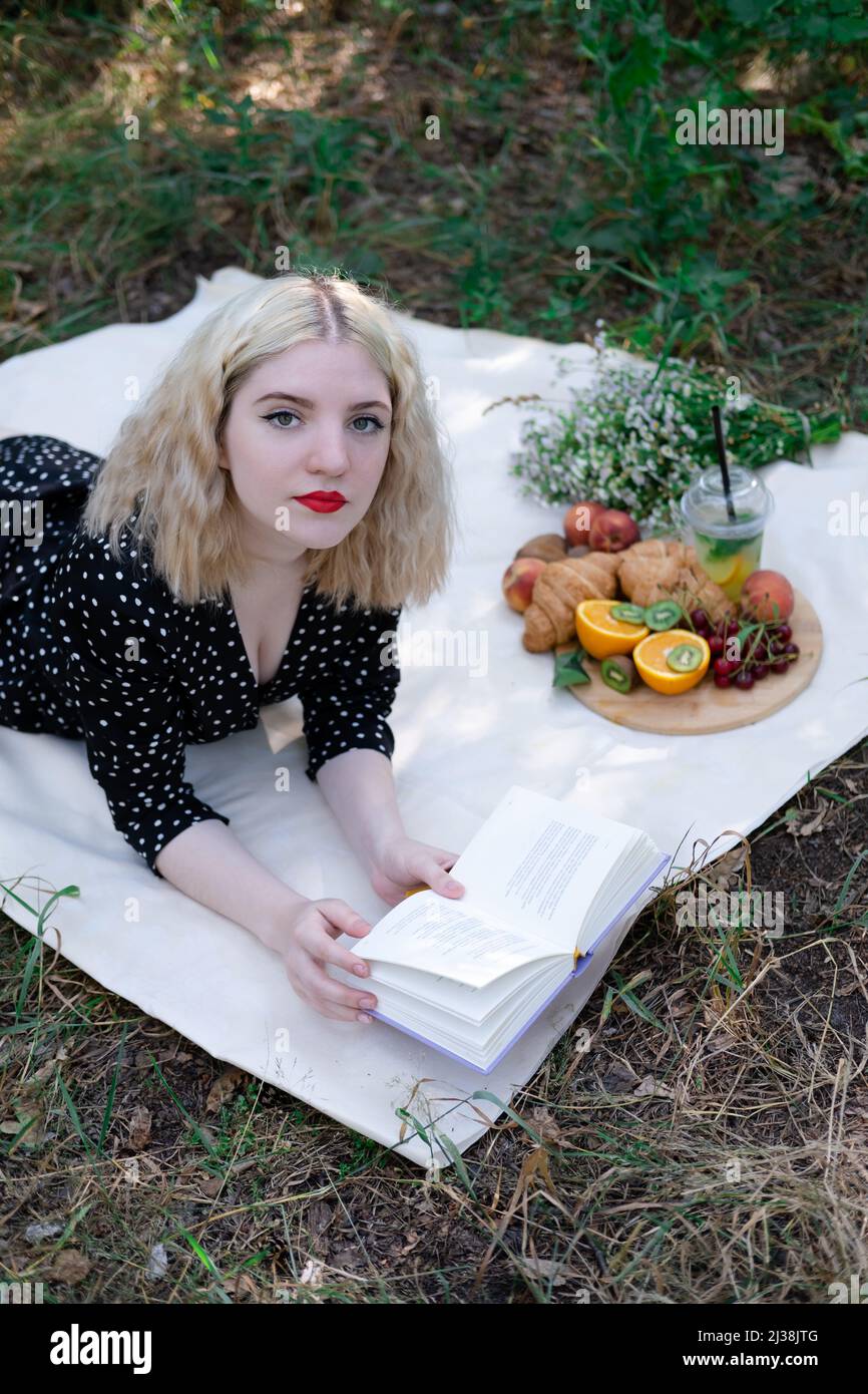charming blonde young woman on a picnic on plaid in park with tasty ...