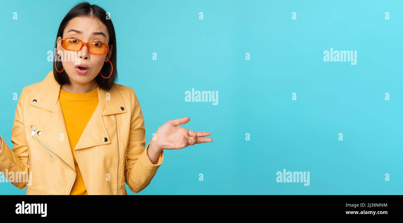 Portrait of chinese girl in sunglasses, looks confused, shrugs ...