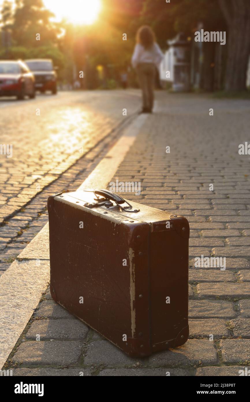 An old suitcase is on the sidewalk of a cobbled street in Italy. In the ...