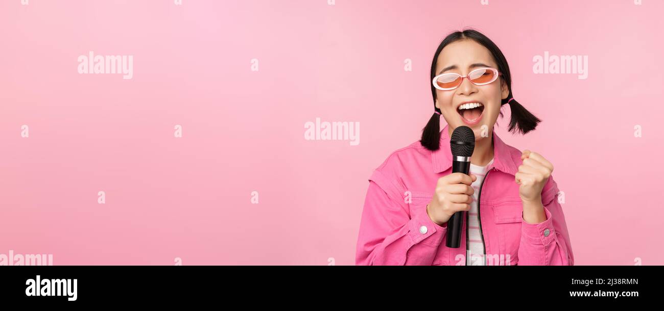Happy beautiful asian girl singing with mic, using microphone, enjoying ...