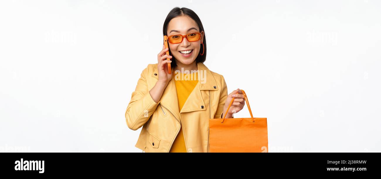 Modern korean girl on shopping, holding store bag, talking on mobile ...