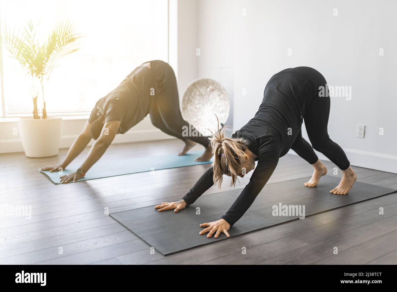 Personal trainer doing yoga pose in sunny studio with client Stock ...