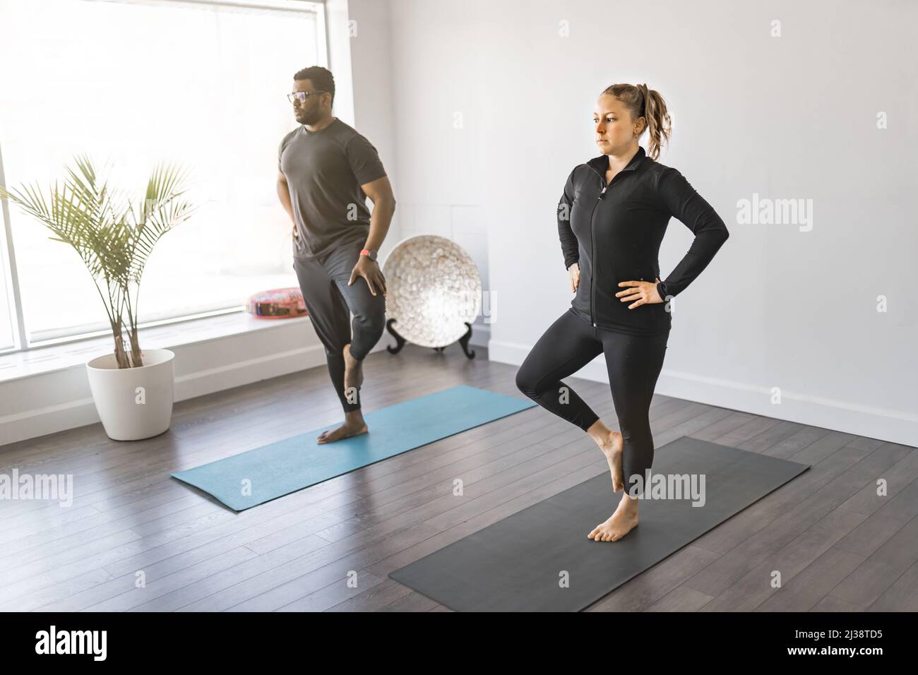 Personal trainer doing yoga pose in sunny studio with client Stock ...