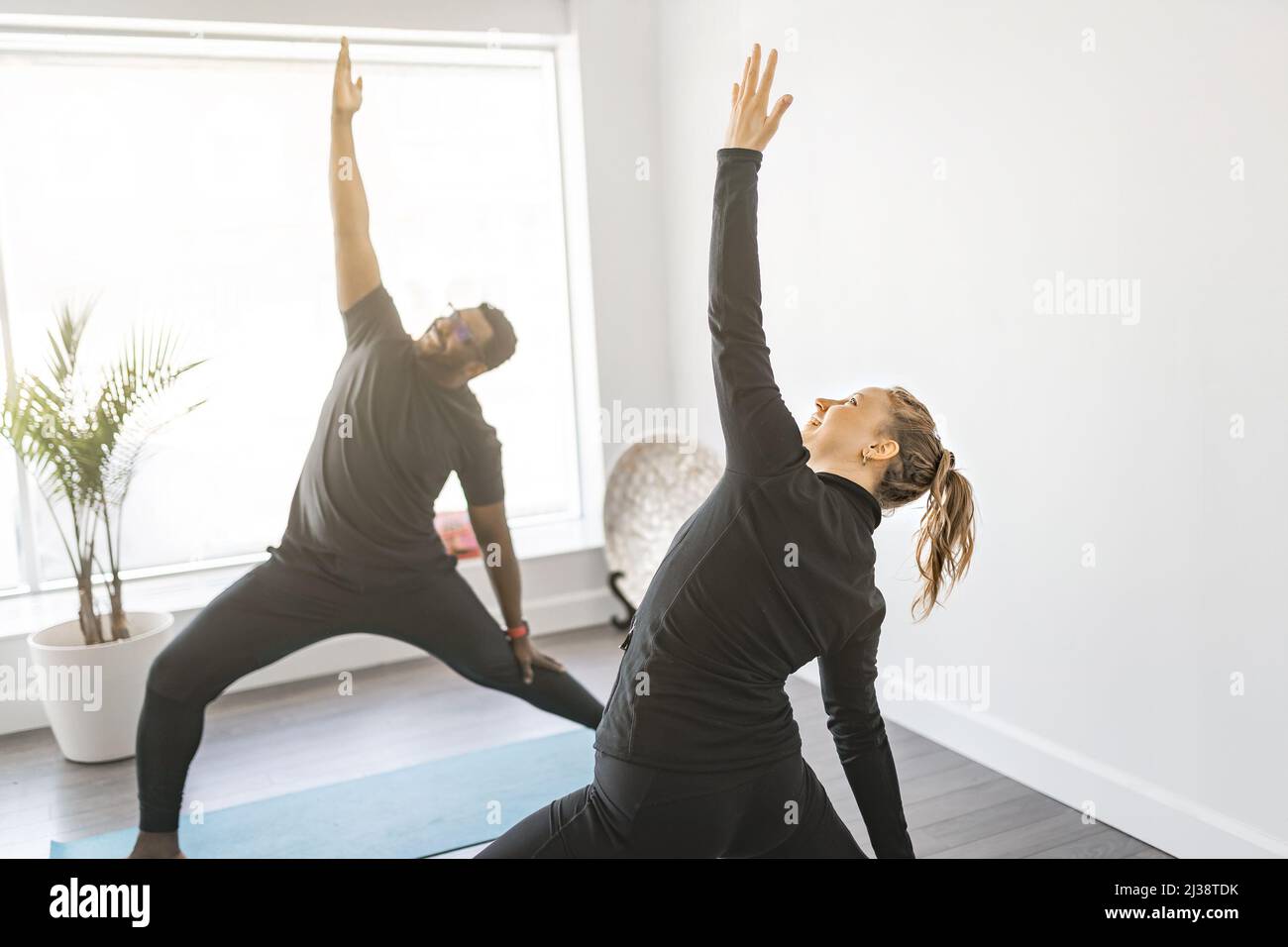 Personal trainer doing yoga pose in sunny studio with client Stock ...