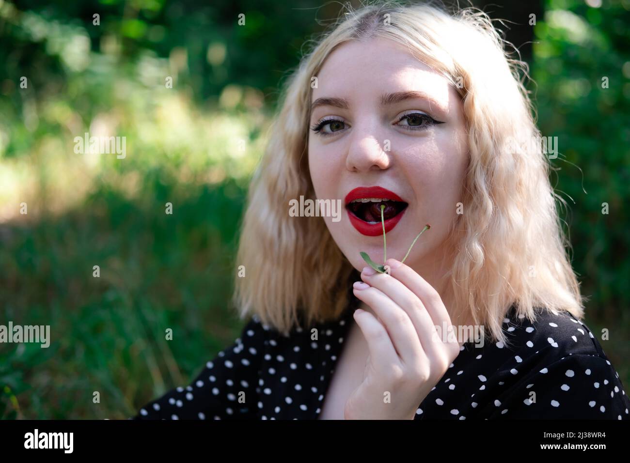 portrait of a charming blonde teenage girl wearing teeth braces biting ...