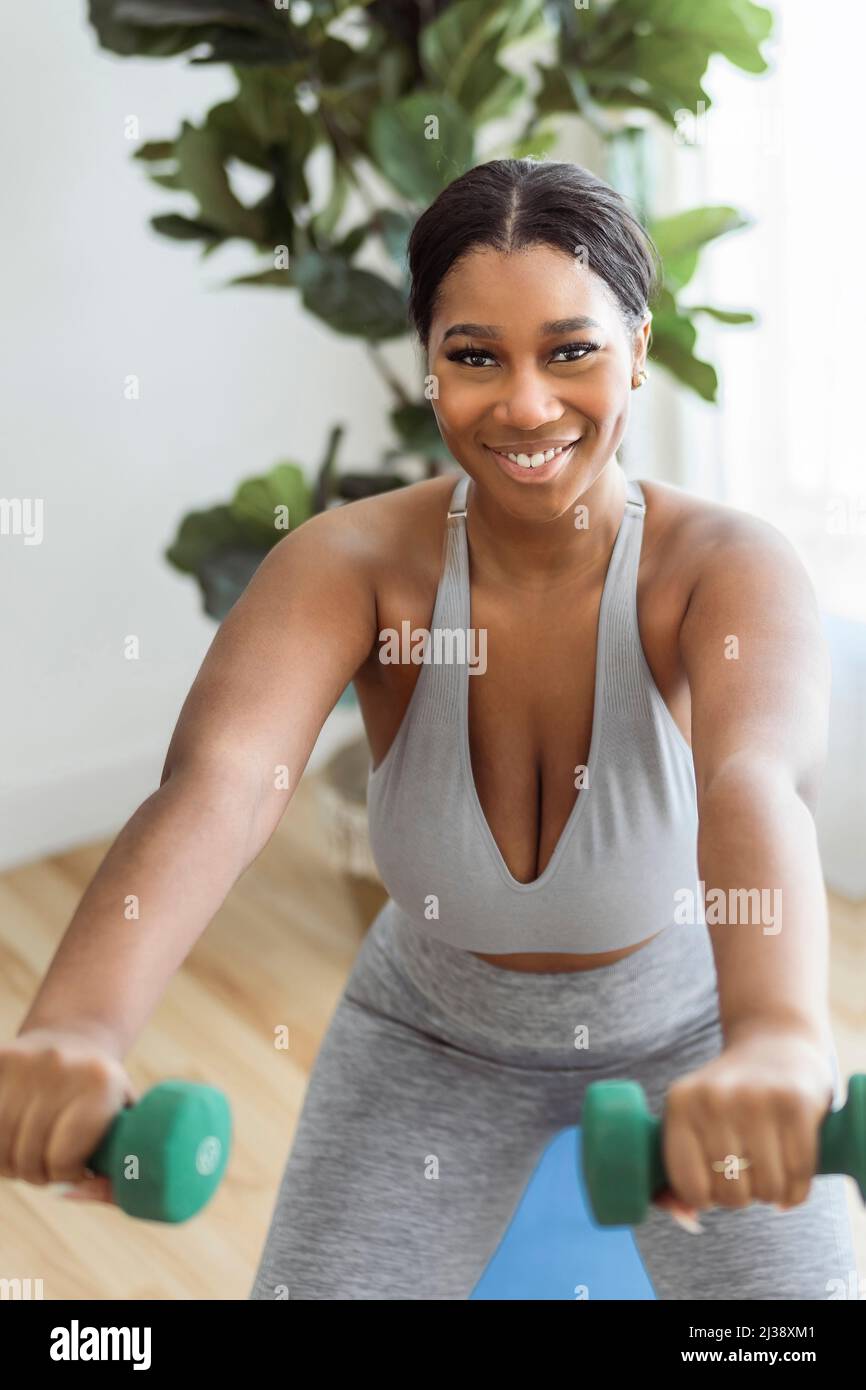 African american woman working out in home livingroom gym lift dumbbell ...